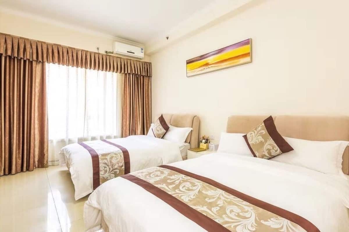 Quarto de hotel com duas camas, cortinas bege, um quadro na parede e um ar condicionado.