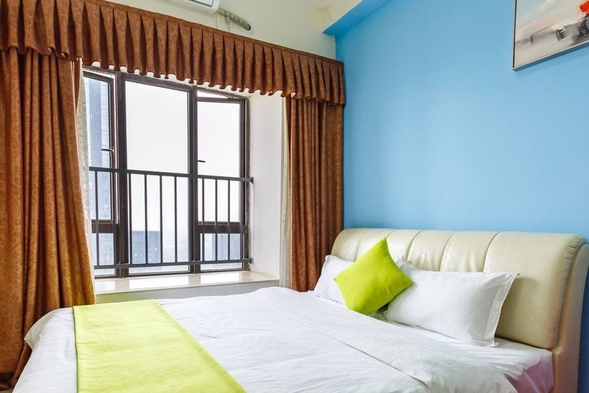 Quarto de hotel com uma cama grande, vista da cidade através de uma varanda e parede azul.