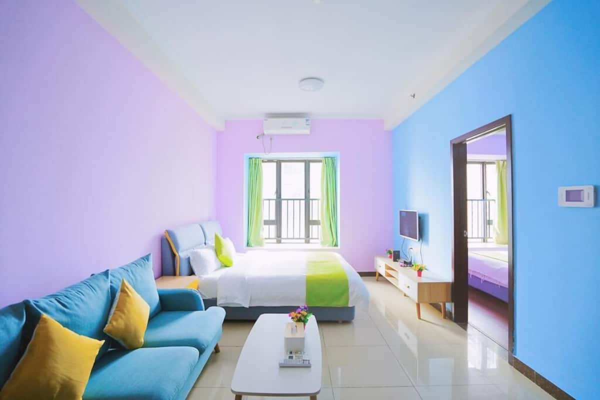 Quarto de hotel moderno com cama, sofá, televisão e uma mesinha.