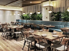 Um restaurante com mesas e cadeiras de madeira, um banco estofado azul e luminárias pendentes.