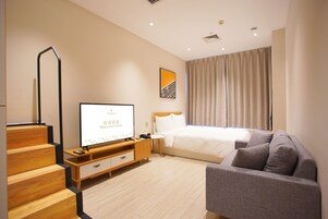 Quarto de hotel moderno com escada de madeira, televisão de tela plana, cama, sofá e uma grande janela com cortinas.