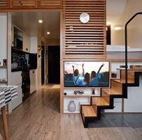 Uma sala de estar moderna com uma TV fixada em uma parede de madeira, uma escada e uma área de cozinha.