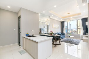 Um apartamento moderno com cozinha, sala de jantar e sala de estar. Possui uma janela grande com vista para a cidade, uma ilha branca na cozinha e um sofá azul na sala de estar.