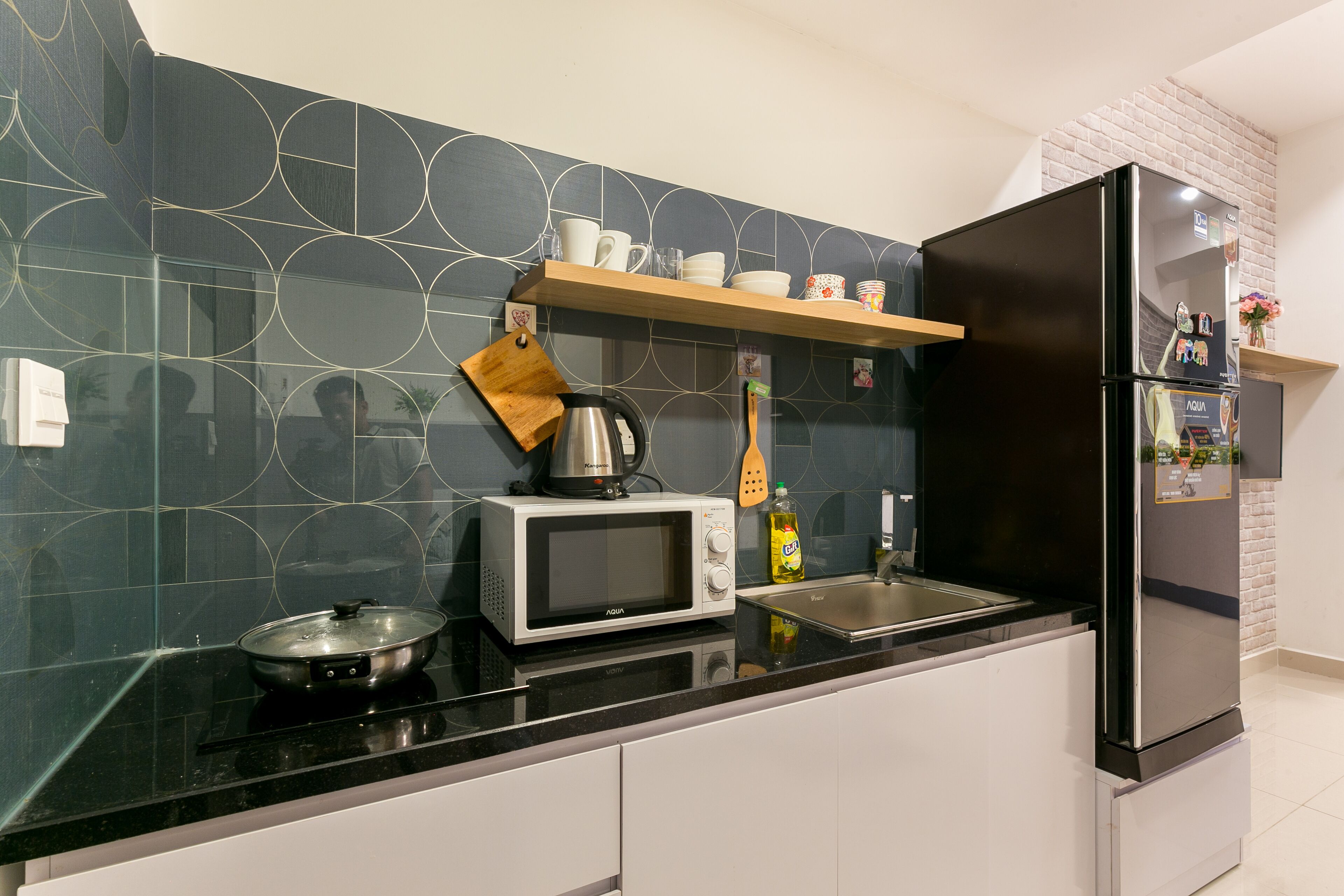 Uma cozinha moderna com geladeira preta, micro-ondas e pia de aço inoxidável.