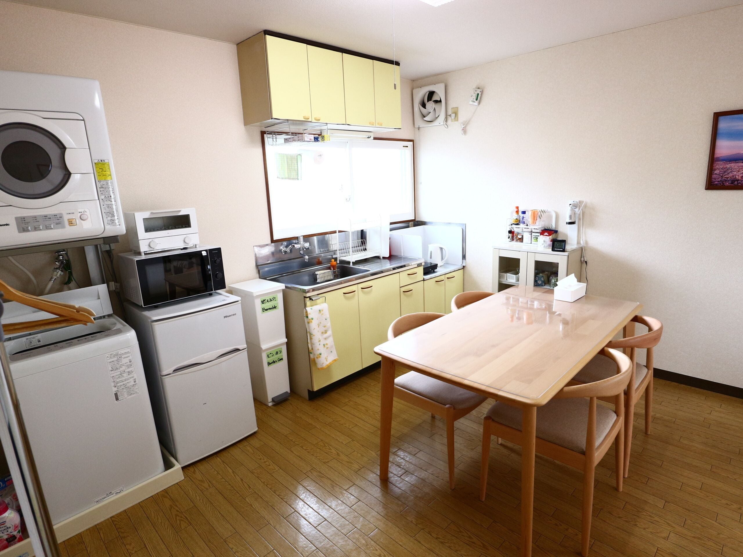 Uma cozinha compacta com micro-ondas, forno e pia. Há uma mesa de jantar com cadeiras e uma pequena geladeira.