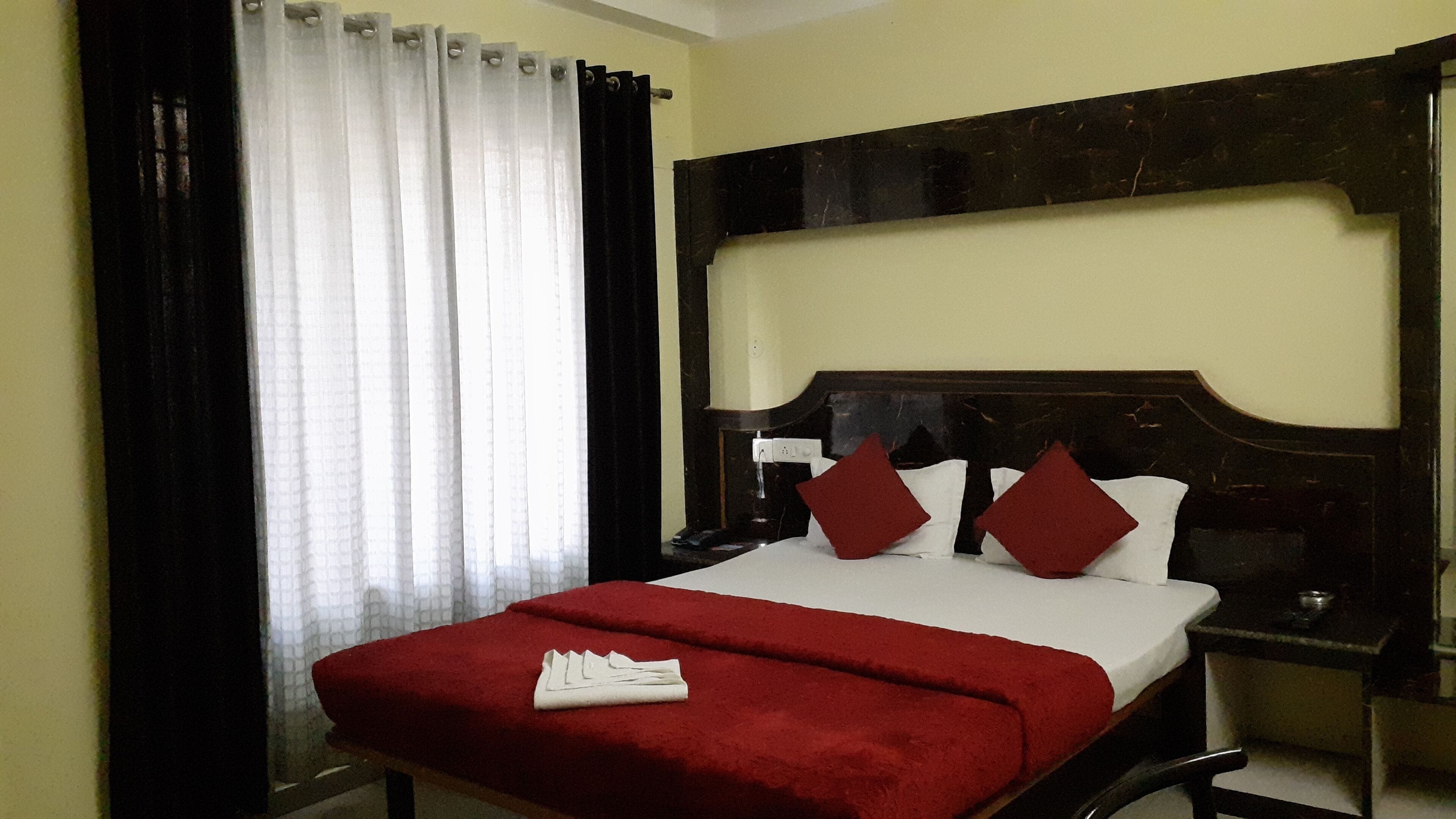 Quarto de hotel com cama, mesa de cabeceira, manta vermelha e travesseiro branco.