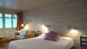 Quarto com cama, duas mesinhas de cabeceira, uma cadeira e duas luminárias na parede.