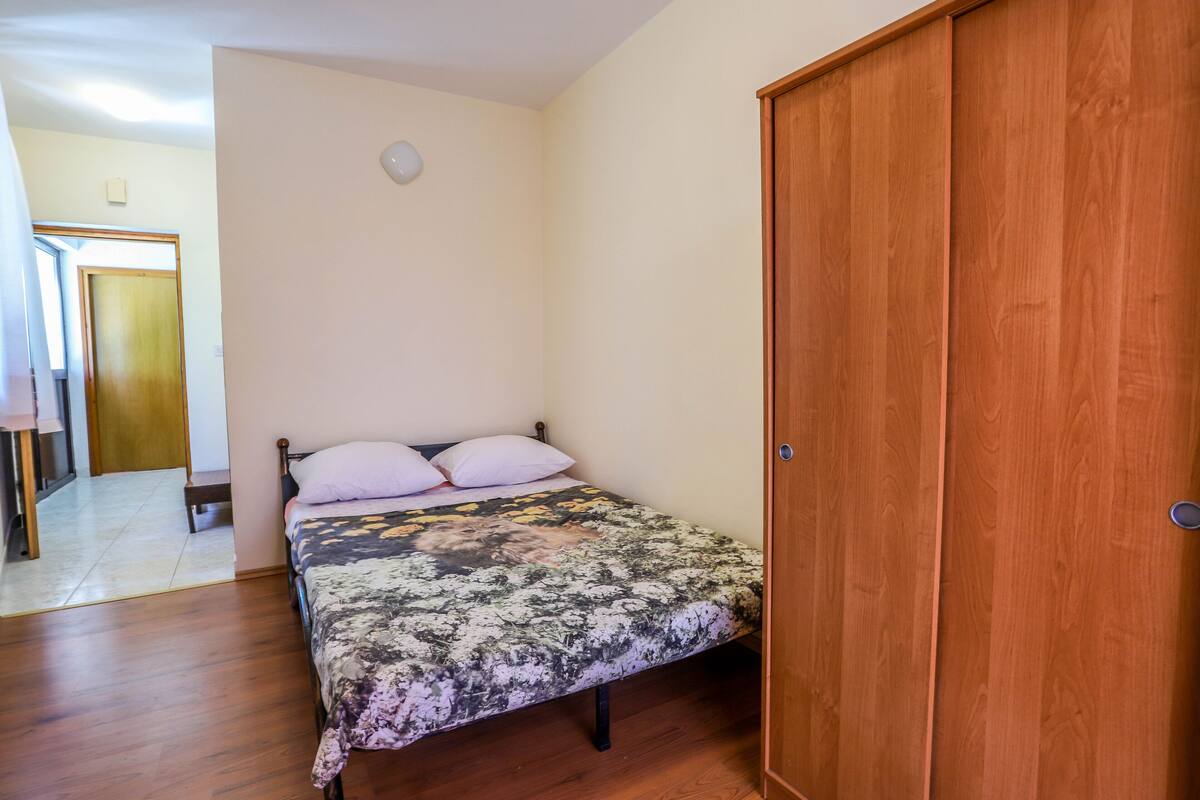 Quarto com cama, guarda-roupa de madeira e porta que dá para outro espaço.