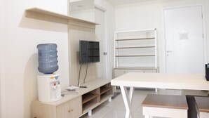 Quarto moderno com escrivaninha branca, TV de tela plana, dispensador de água e quadro branco na parede.
