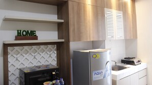 Uma cozinha com geladeira, micro-ondas e pia. Há uma prateleira de madeira com uma placa de 'HOME' e um objeto decorativo.