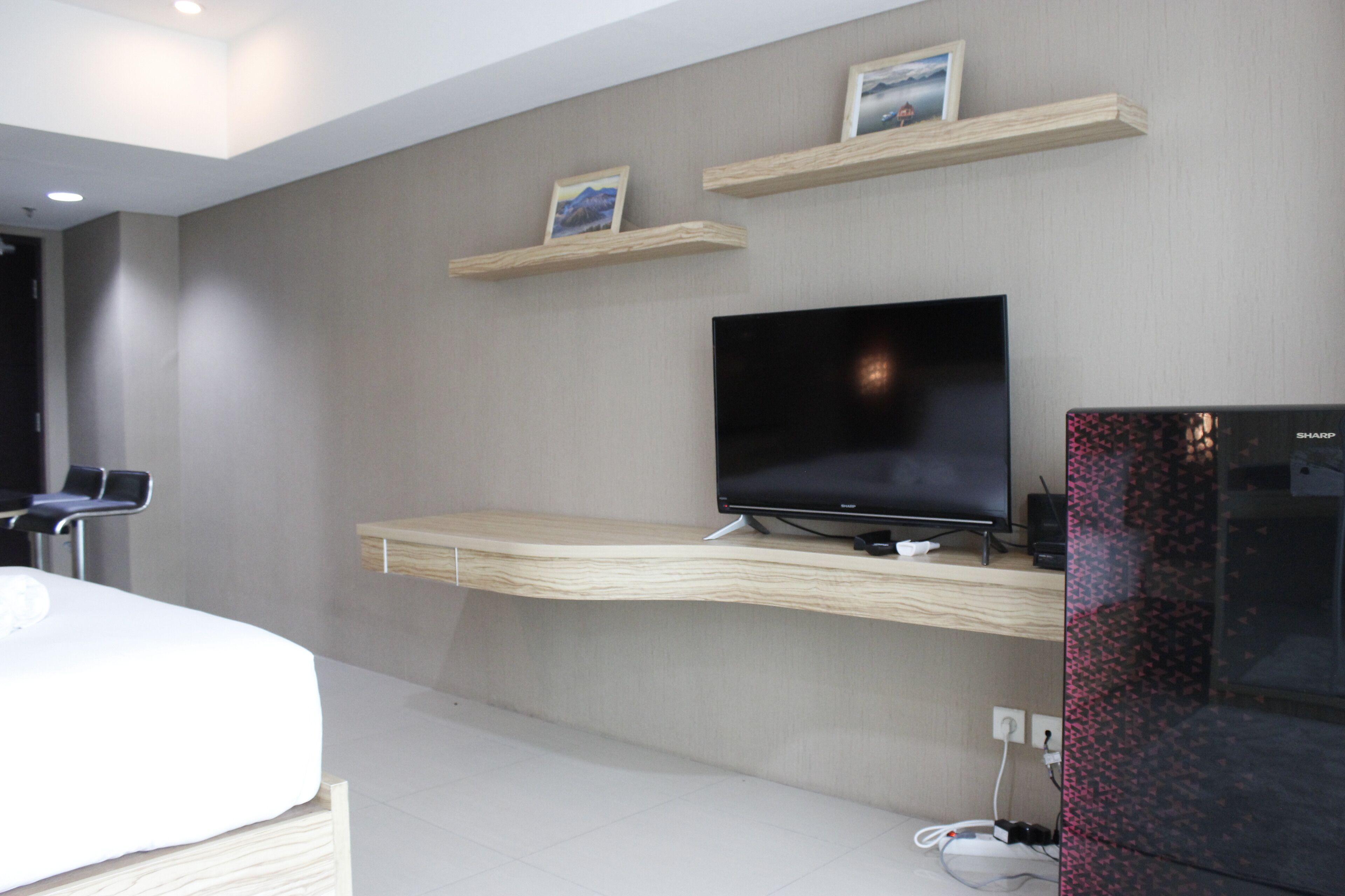 Quarto de hotel moderno com cama, televisão de tela plana fixada em console de madeira e geladeira.