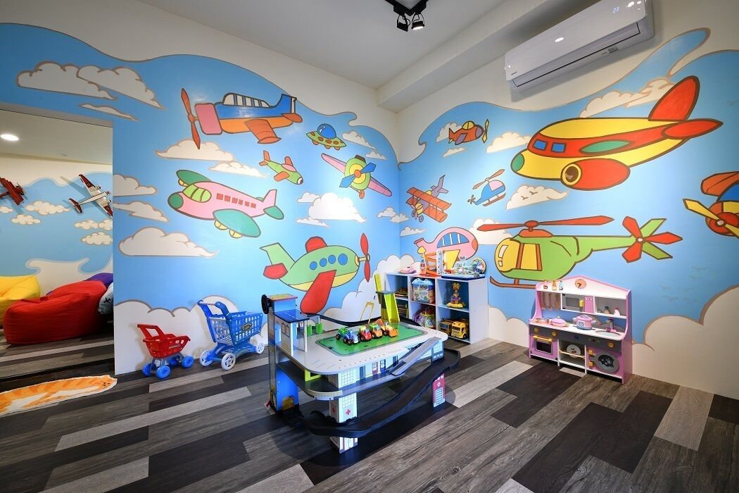 Uma sala de brincar com um mural colorido de um avião, um conjunto de trem de brinquedo e uma casinha.