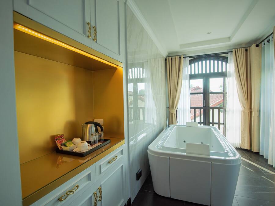 Um banheiro moderno com uma banheira grande, uma pia com um porta-objetos e vista para o exterior através de uma janela com cortinas.