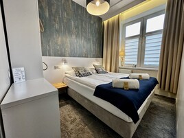 Quarto de hotel moderno com uma cama grande, abajures, mesa de cabeceira, janela com cortinas e parede com design texturizado.
