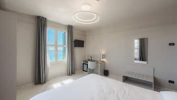 Quarto de hotel moderno com uma cama grande, uma escrivaninha, uma cadeira, uma televisão e uma janela com cortinas.