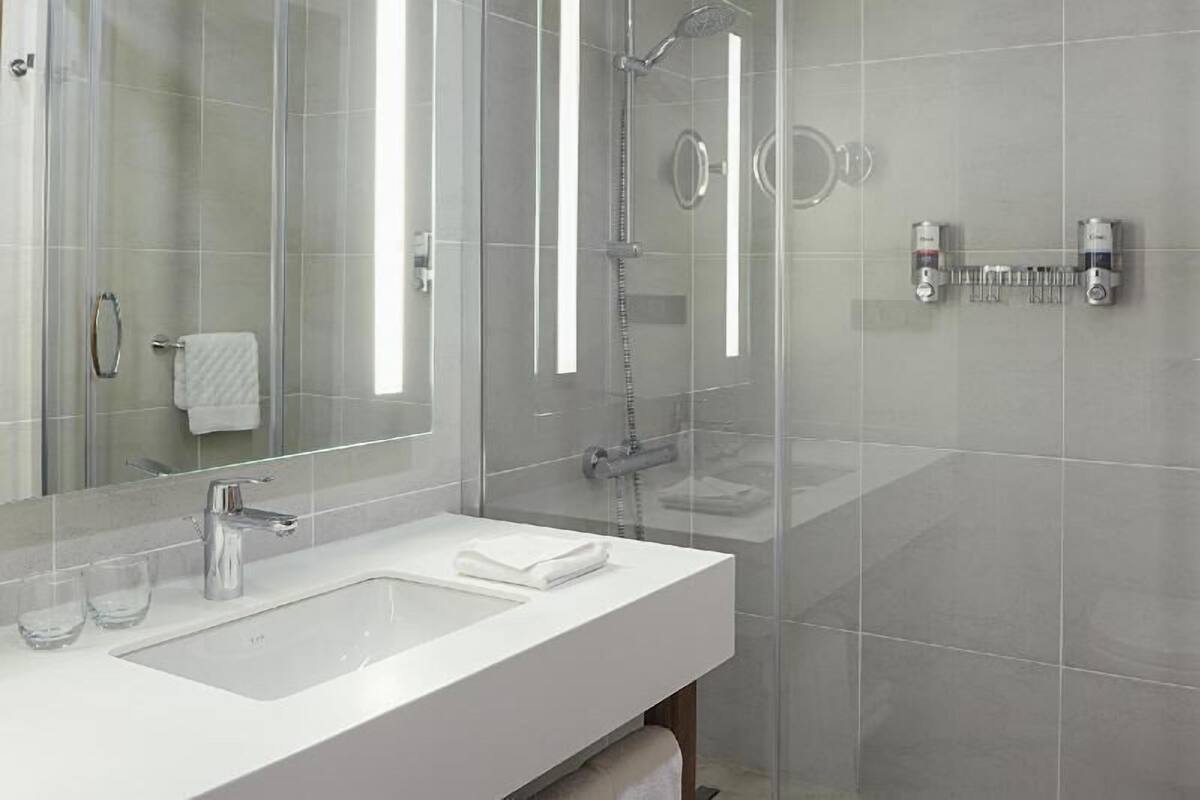 Uma casa de banho moderna com cabine de duche em vidro, lavatório branco e espelho grande.