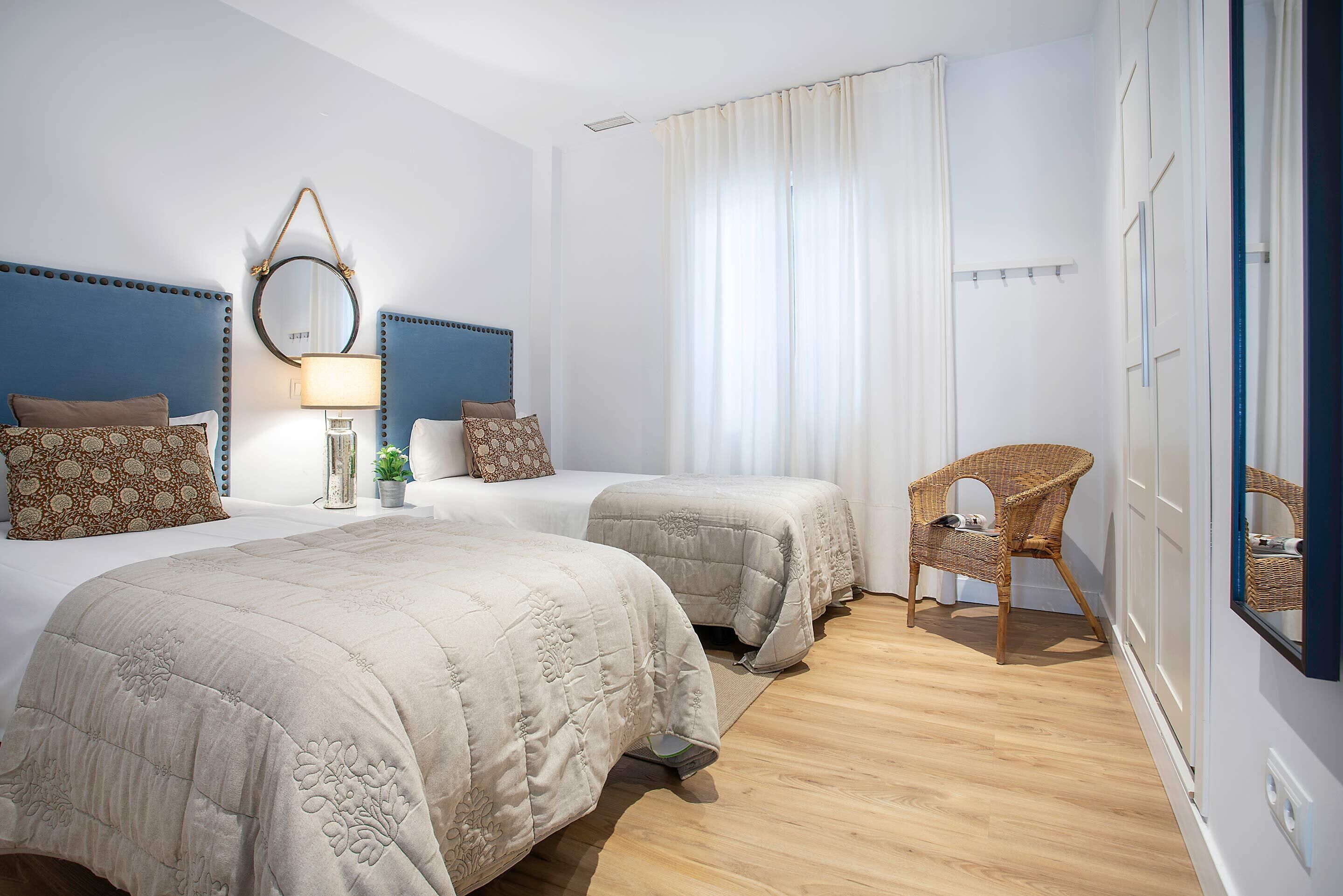 Quarto de hotel com duas camas, uma cadeira, um abajur e um espelho grande.