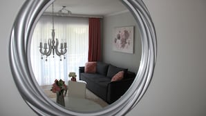 Uma sala de estar com um sofá preto, uma mesa de centro branca, um vaso com flores, um candelabro e um quadro na parede.