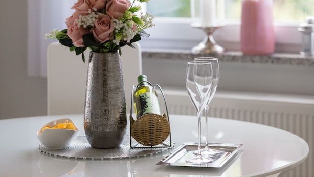 Uma mesa com um vaso de flores, uma garrafa, um copo e uma tigela.