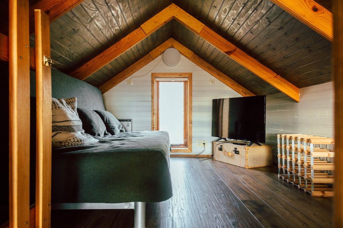 Um quarto de sótão acolhedor com uma cama, vigas de madeira, uma televisão e uma mala.