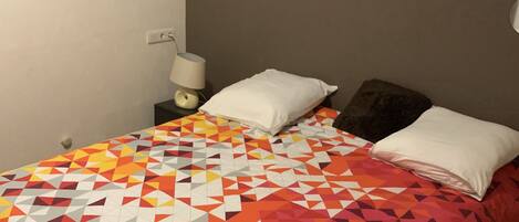 Quarto com cama, almofadas, mesa de cabeceira, abajur e decorações nas paredes.