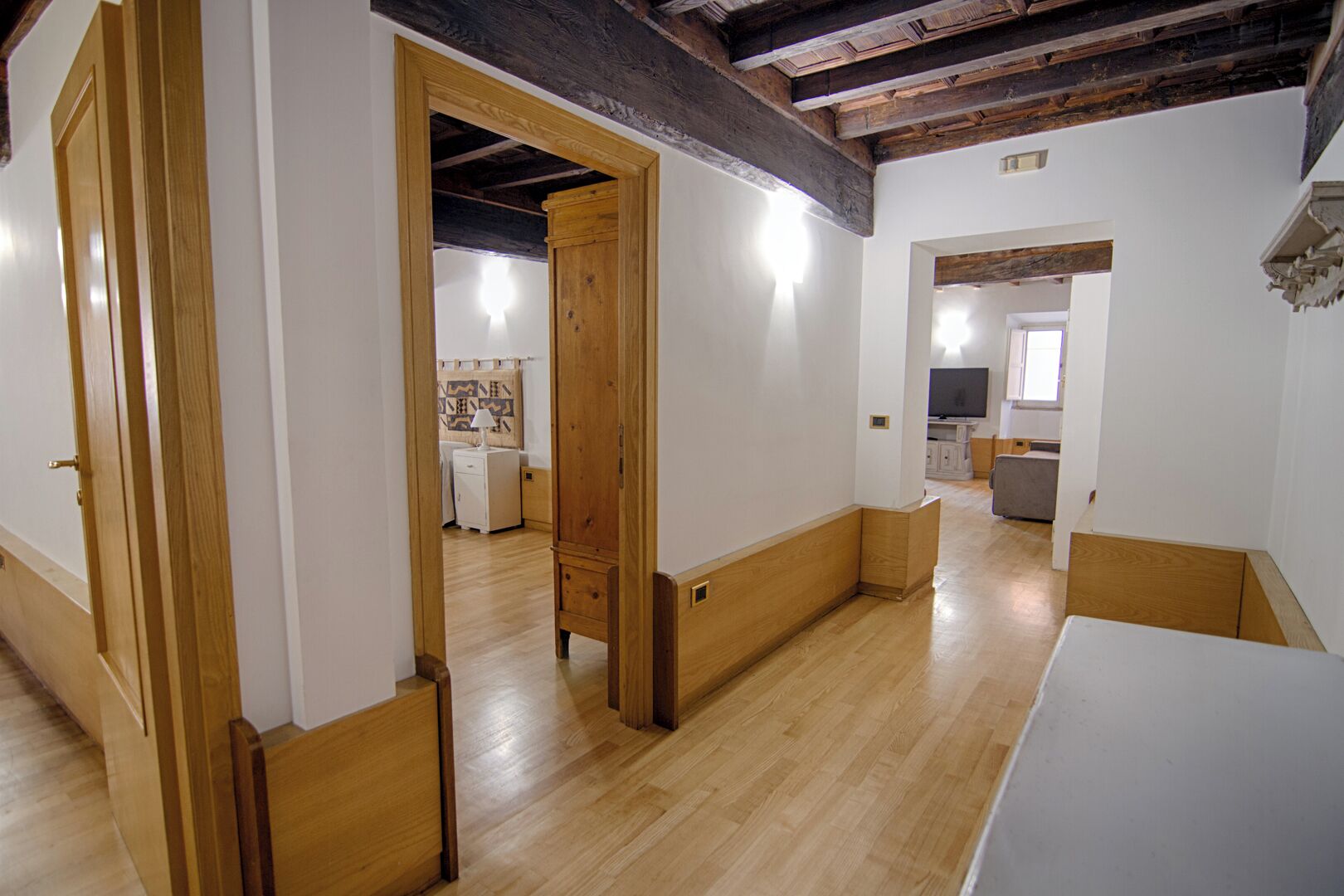 Quarto amplo com soalho de madeira, teto branco e vigas expostas.
