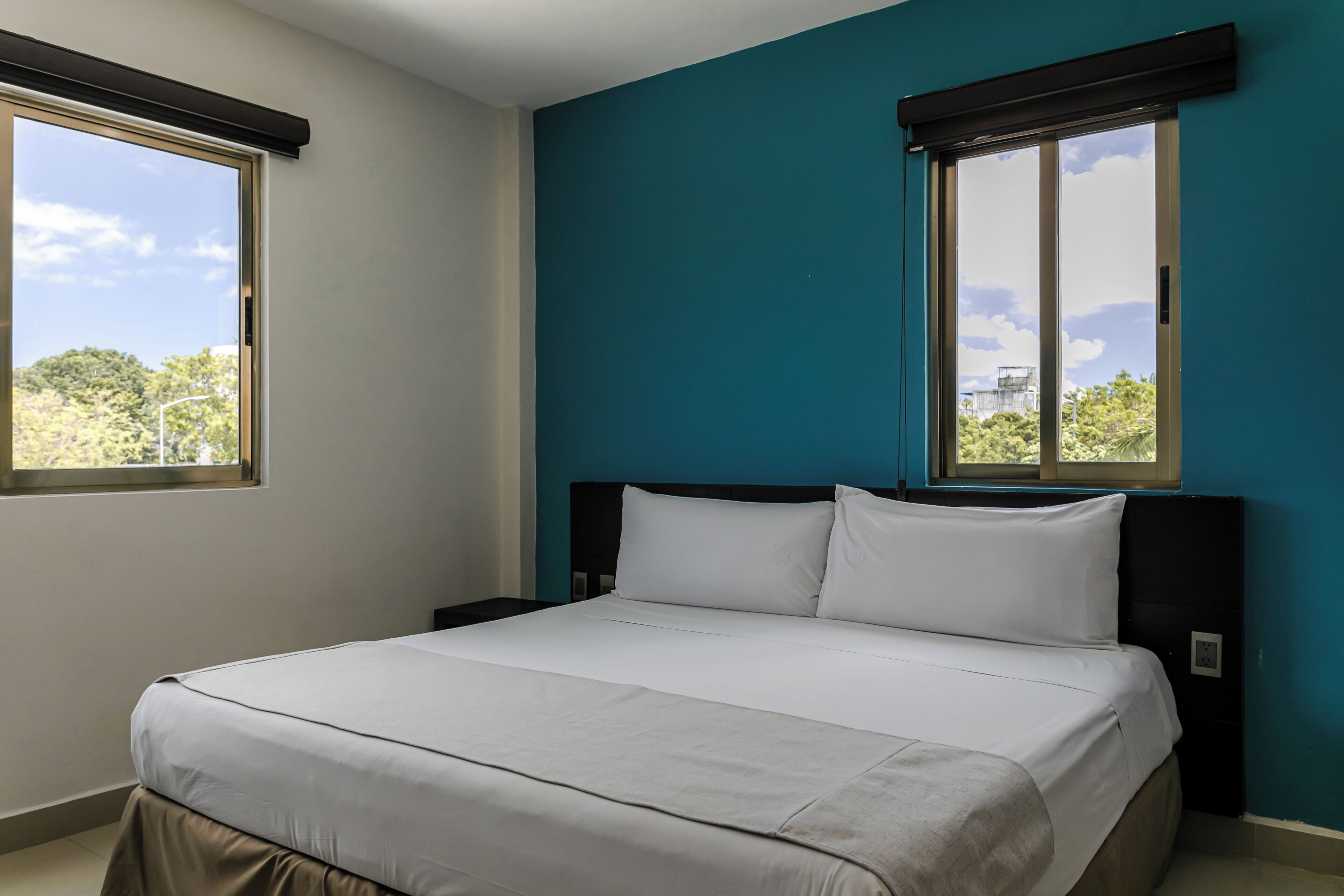 Quarto com cama, duas janelas e parede azul-turquesa.