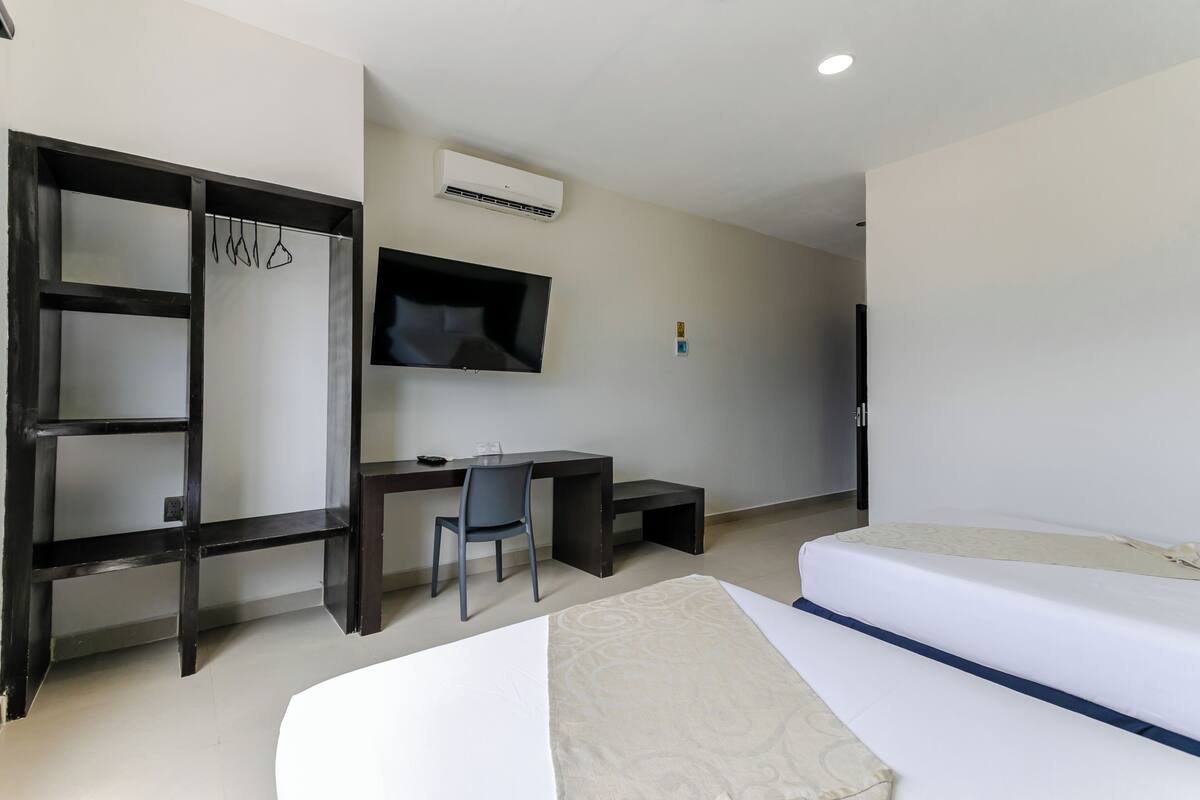 Quarto com cama, escrivaninha, cadeira, televisão e ar condicionado.
