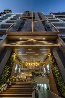 Entrada de hotel com design moderno, apresentando uma escadaria que leva ao saguão, fachada de vidro e uma placa com o nome do hotel.