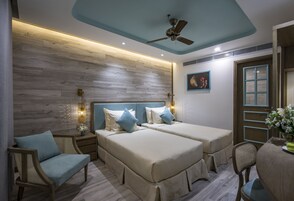 Quarto de hotel moderno com duas camas, um ventilador de teto, parede de detalhes em madeira e área de refeições com mesa e cadeiras.