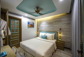 Quarto com cama, mesas de cabeceira, ventilador de teto, luminária na parede e piso de madeira.