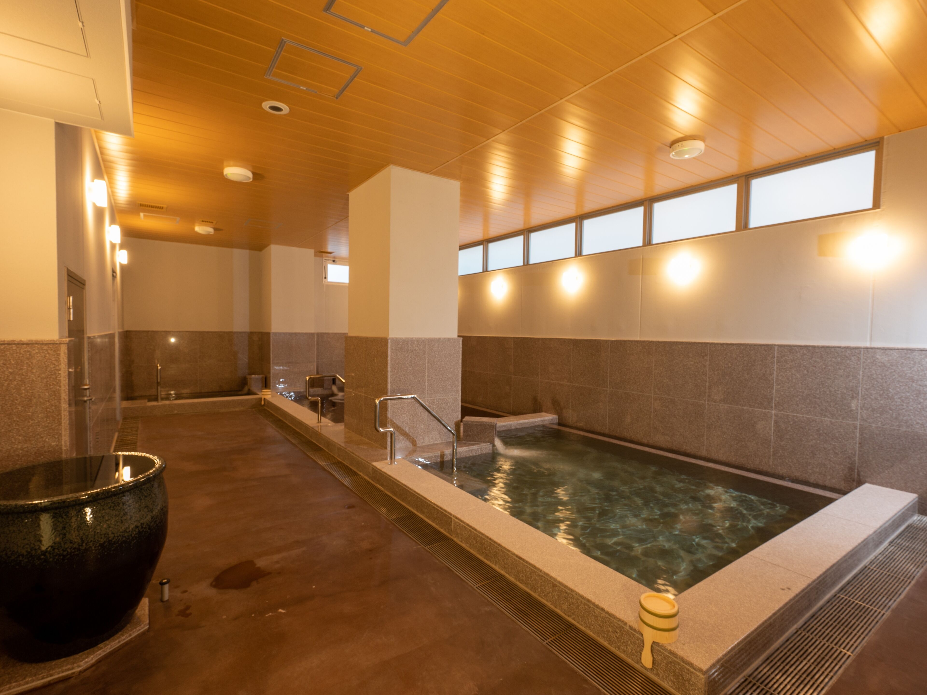 Uma área de spa com uma banheira de hidromassagem, uma grande bacia de pedra e uma parede revestida com janelas.