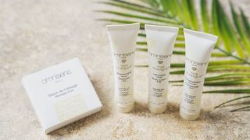 Três tubos de produtos Omnisens e uma caixa de sabonete de massagem sobre uma superfície texturizada, com uma folha de palmeira ao fundo.