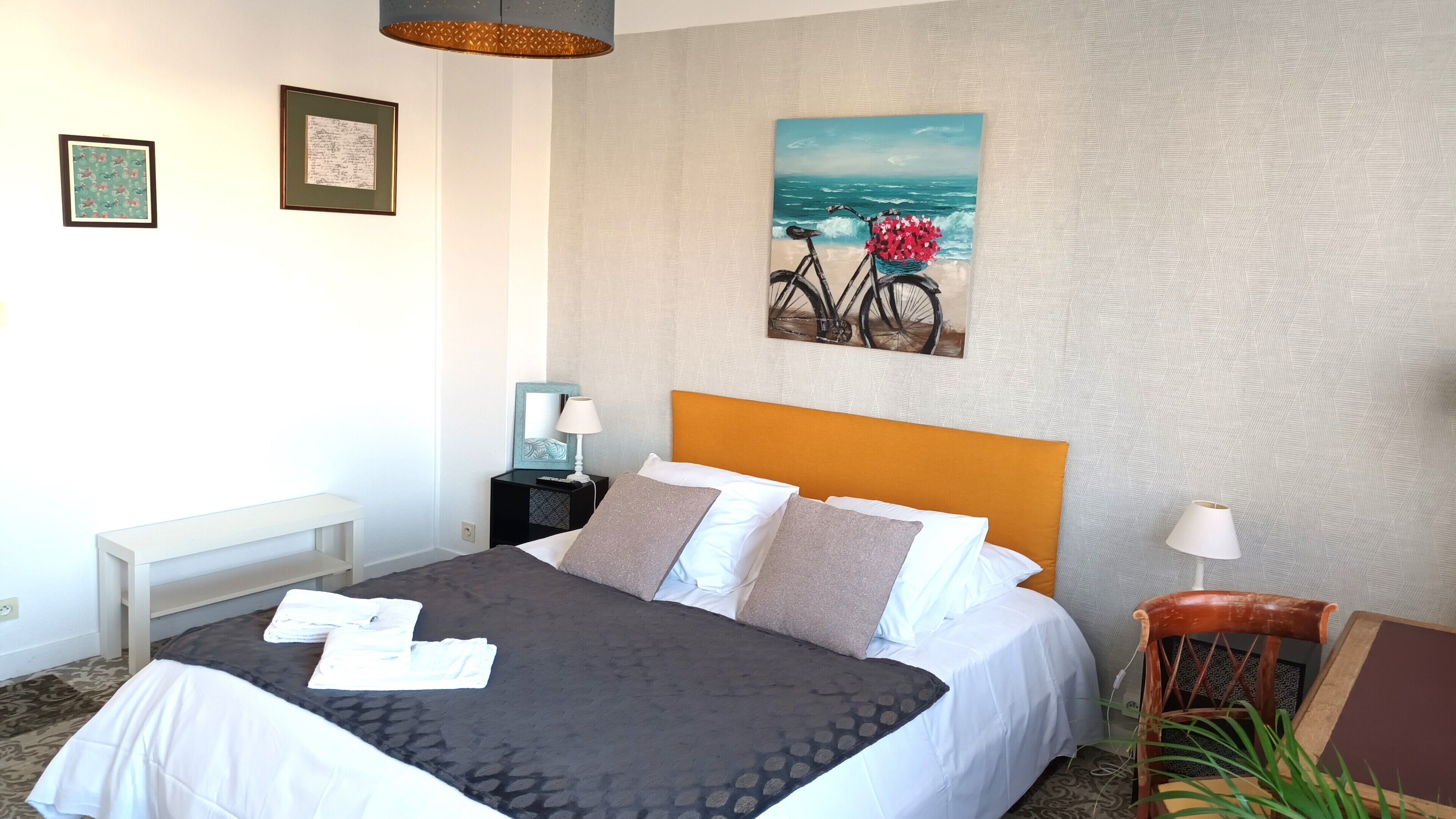 Quarto de hotel com uma cama, mesa de cabeceira, cadeira e um quadro de bicicleta na parede.