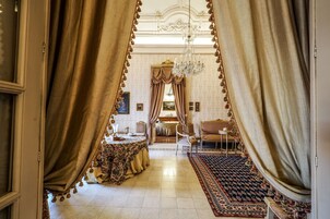 Um quarto luxuoso com uma cama grande, cortinas elaboradas, um candelabro e um tapete estampado.