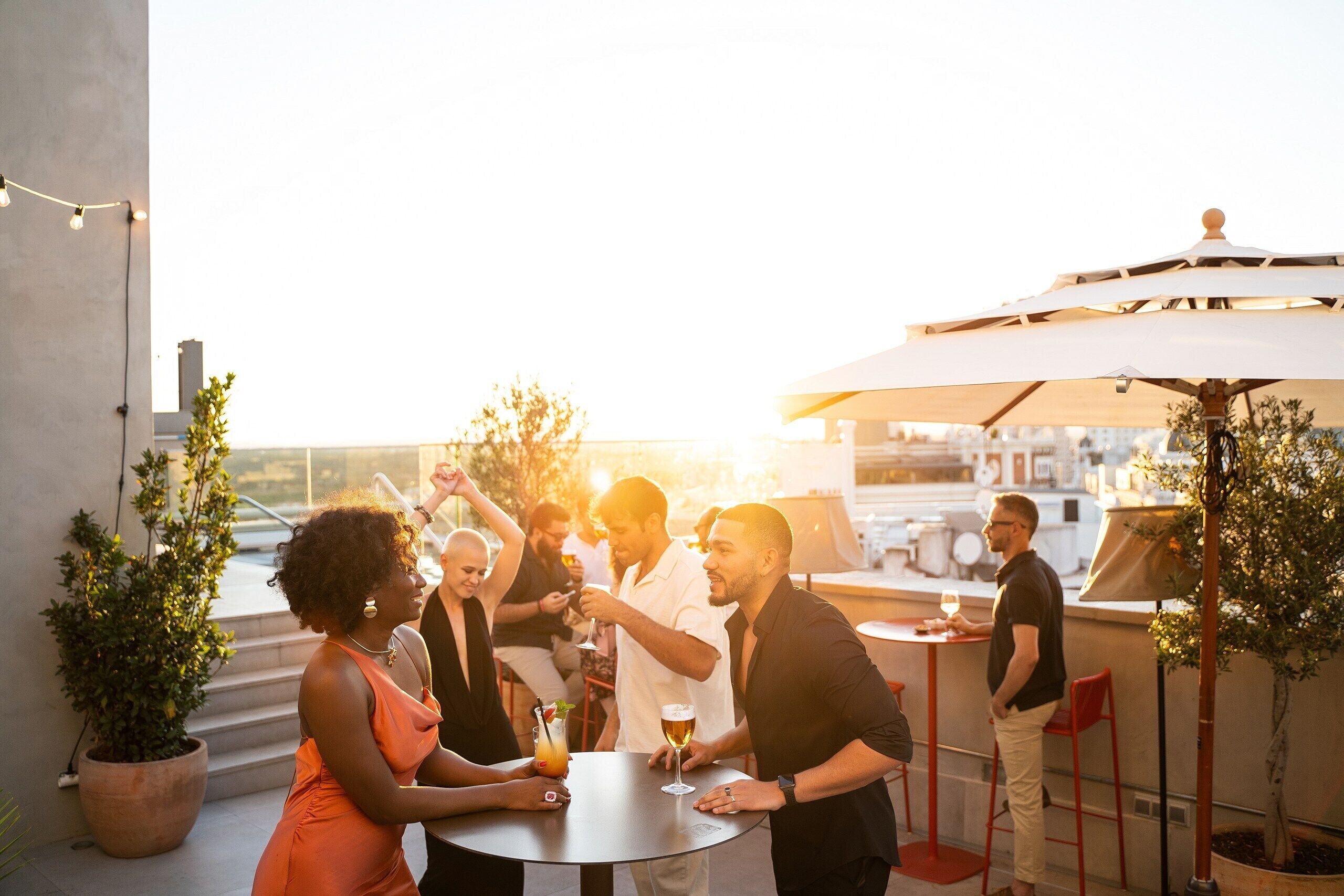 Um bar no terraço com mesas ao ar livre, plantas em vasos e vista para o horizonte da cidade.