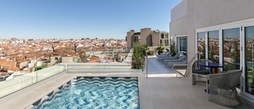 Piscina no terraço com vista para a cidade, cadeiras de descanso e área envidraçada.