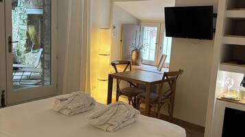 Quarto de hotel com uma cama grande, uma mesa de jantar com cadeiras, uma televisão fixada na parede e uma pequena cozinha.