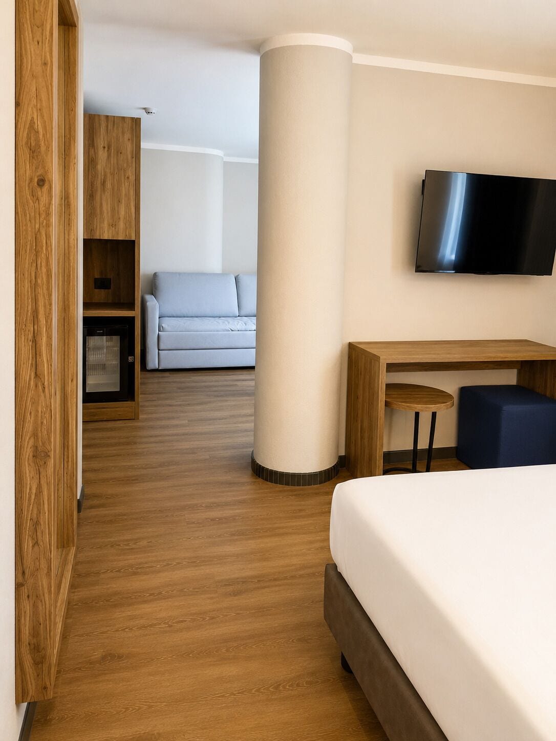 A hotel room with a bed, a desk, a television, a sofa, and a wooden wardrobe.