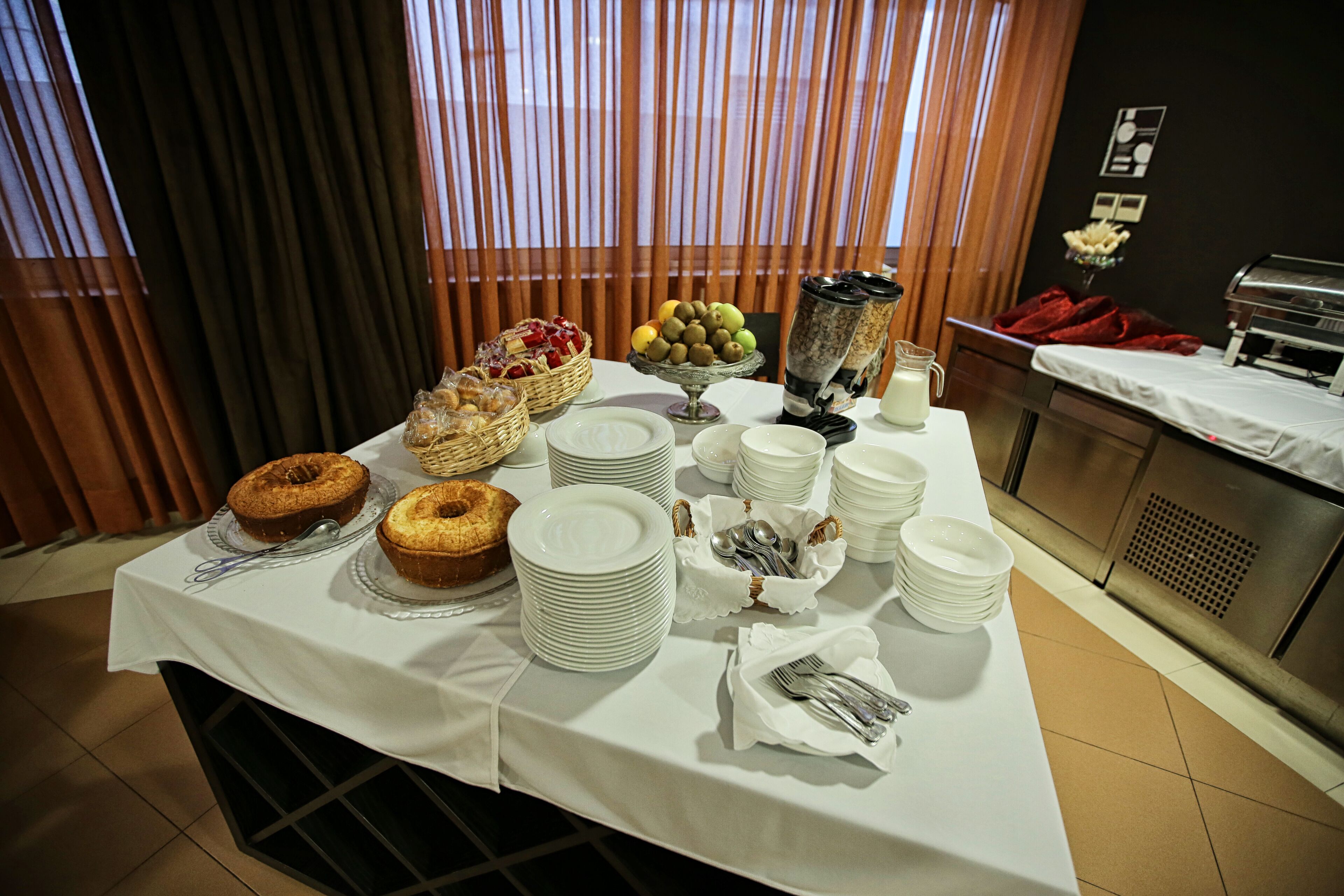 Disposição de buffet com diversos alimentos, pratos e utensílios sobre uma mesa.