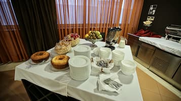 Disposição de buffet com diversos alimentos, pratos e utensílios sobre uma mesa.