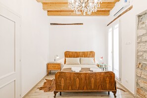 Quarto com cama de madeira, um lustre, parede de pedra e uma janela grande.