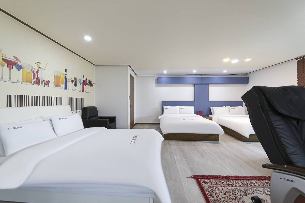 Quarto de hotel com duas camas, uma grande obra de arte na parede retratando bebidas e um tapete vermelho estampado.