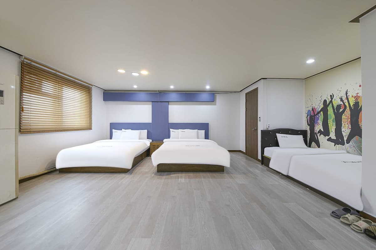 Quarto de hotel com duas camas, uma janela grande com persianas, um mural na parede e piso de madeira.
