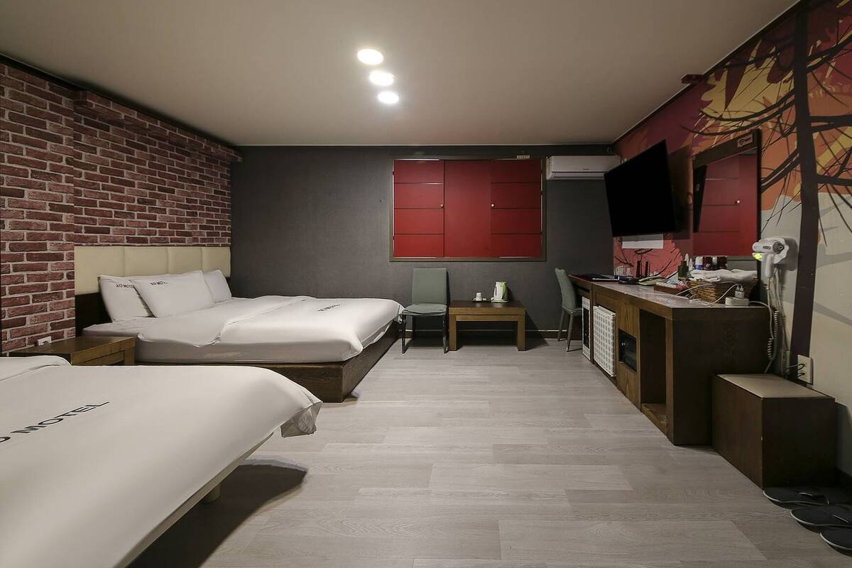 Quarto de hotel com duas camas, uma escrivaninha, uma cadeira, uma televisão e um banheiro.