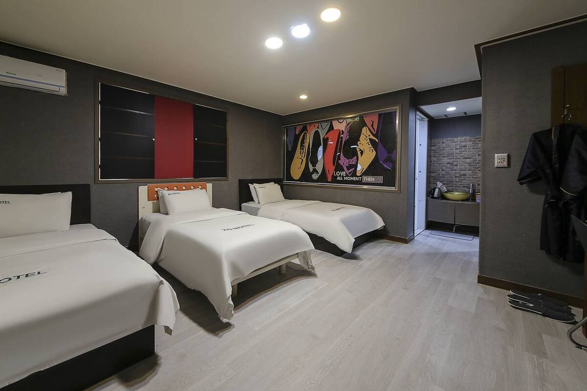 Quarto de hotel com duas camas, uma janela grande, um cartaz, uma pia e um roupão.