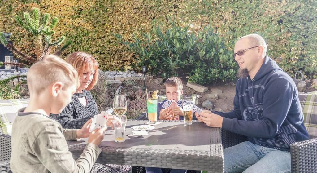 Um grupo de pessoas sentadas numa mesa ao ar livre, com bebidas e cartas, rodeadas por vegetação.