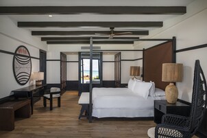 Quarto de hotel moderno com cama, escrivaninha, cadeira e vista para a praia.