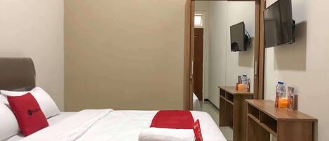 Quarto de hotel com uma cama, uma mesa de cabeceira de madeira, um espelho e uma televisão.