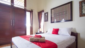 Quarto de hotel com uma cama grande, um guarda-roupa de madeira, uma mesa de cabeceira com luminária e uma tapeçaria emoldurada na parede.